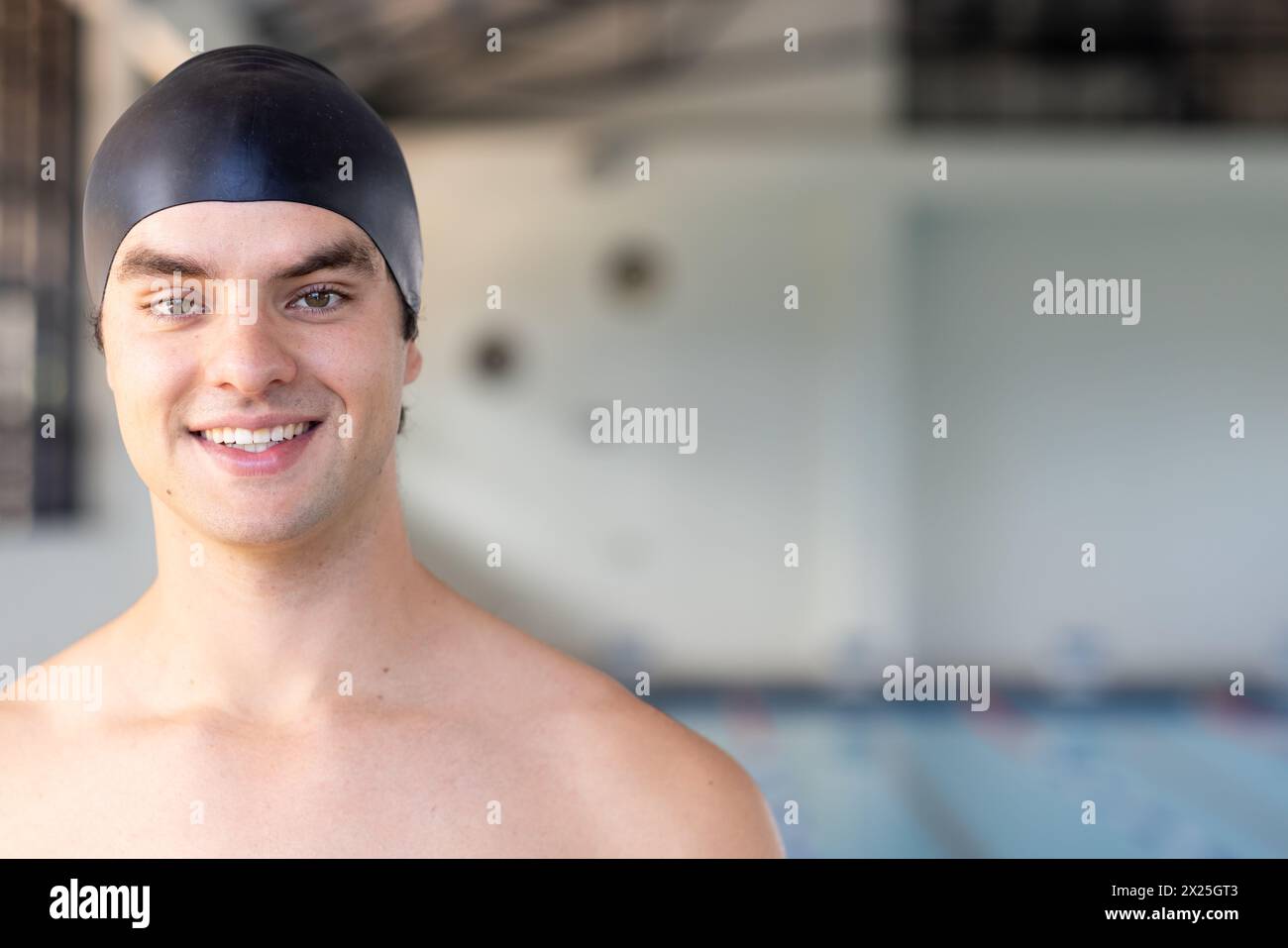 Caucasian young male swimmer standing by pool indoors, wearing cap ...