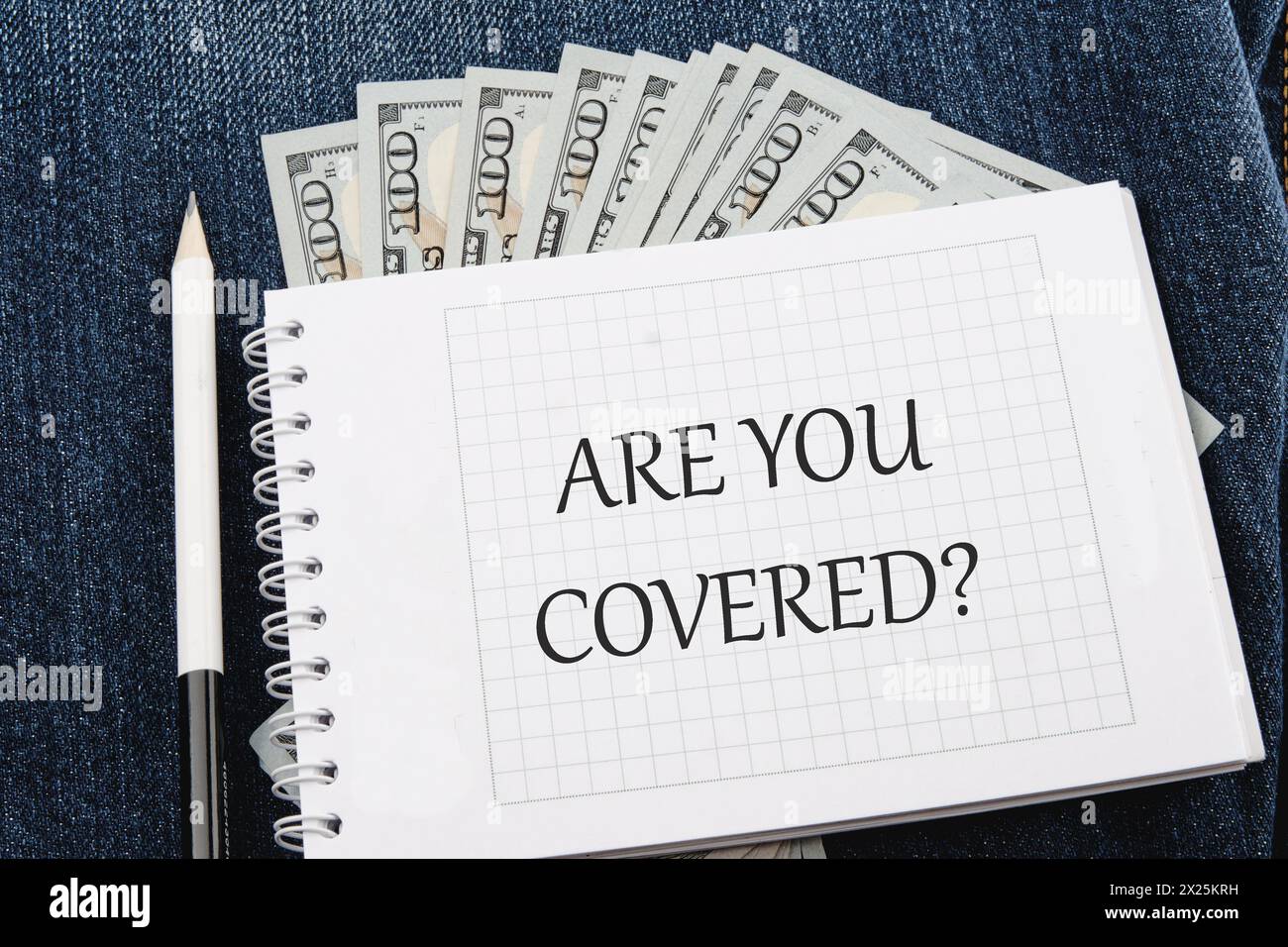 ARE YOU COVERED text written on a notebook lying on jeans with dollar ...