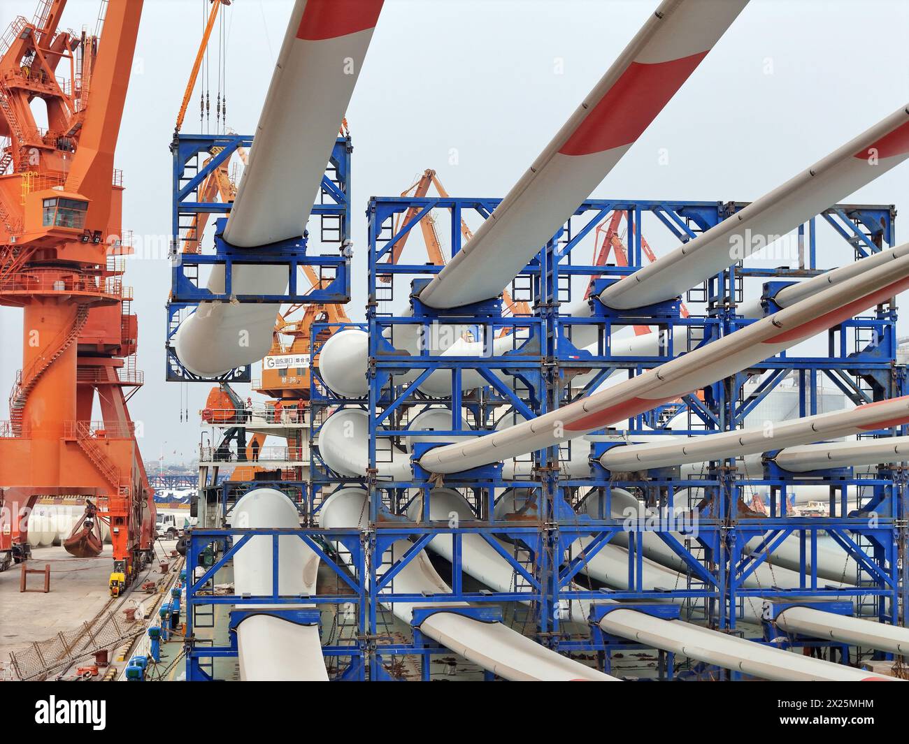YANTAI, CHINA - APRIL 19, 2024 - A crane loads offshore wind turbine blades for a cargo ship at ...