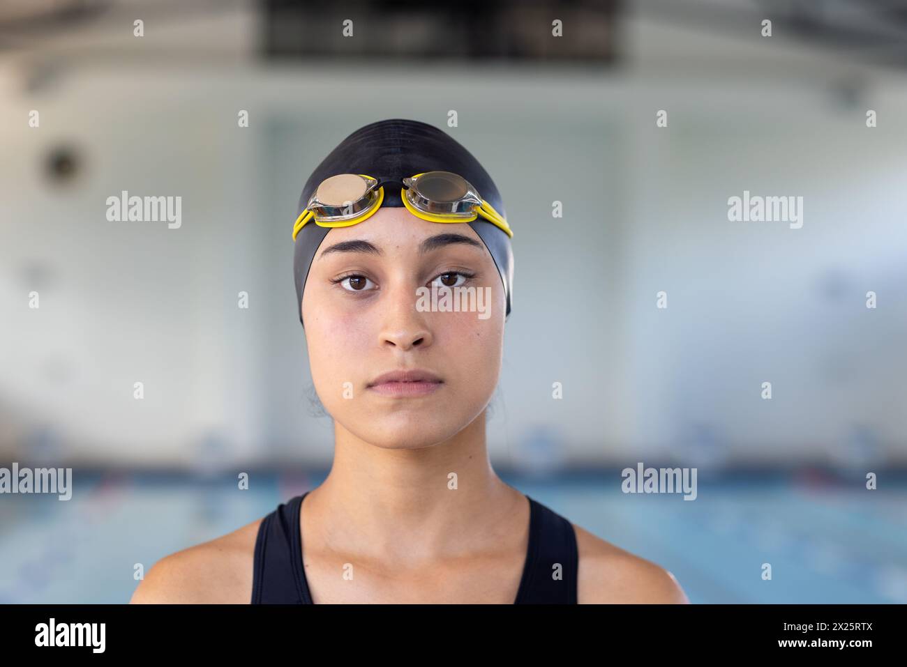 Biracial young female swimmer standing indoors in front of a pool ...