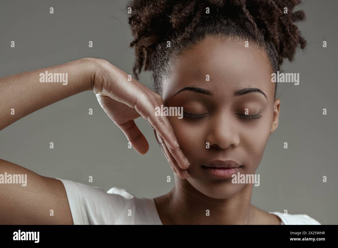 Serene young black woman with closed eyes, hand gently touching face ...