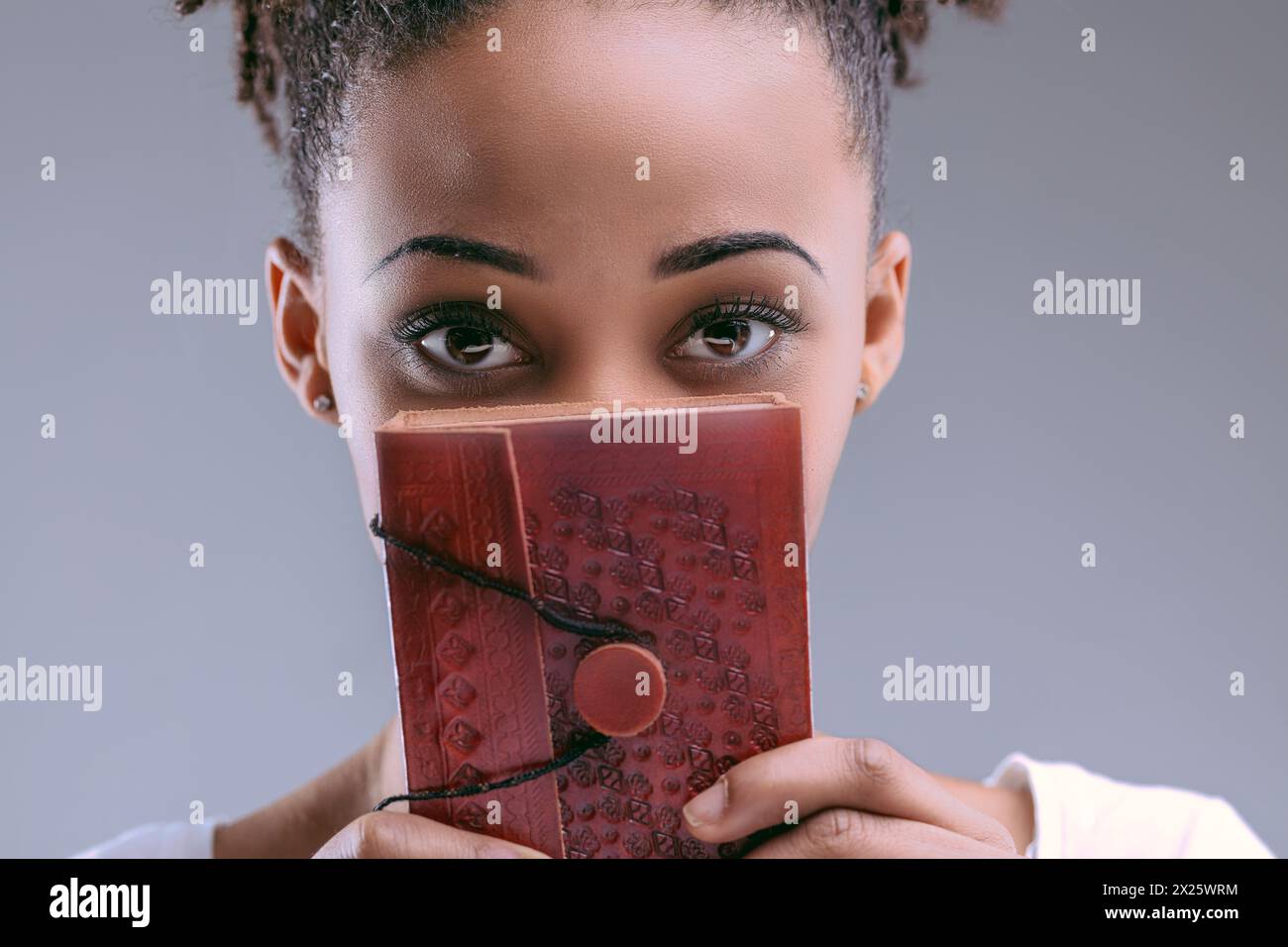 Young woman with enigmatic eyes peers over a richly embossed red ...