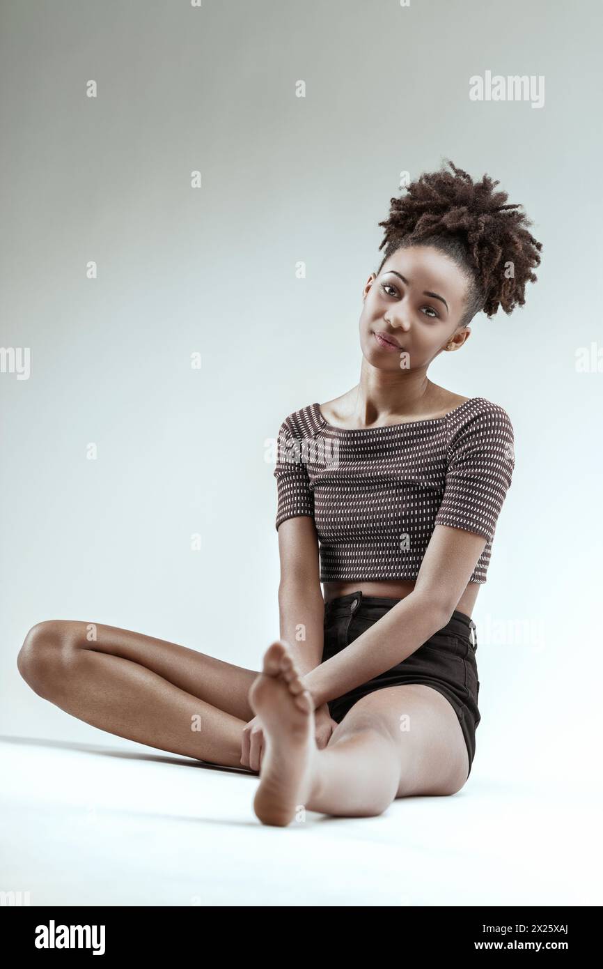 Comfortable in her style, a young woman lounges with a soft expression ...