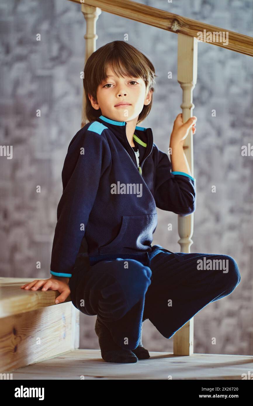 Sad white boy, 7 years old, squats on step of wooden staircase and ...