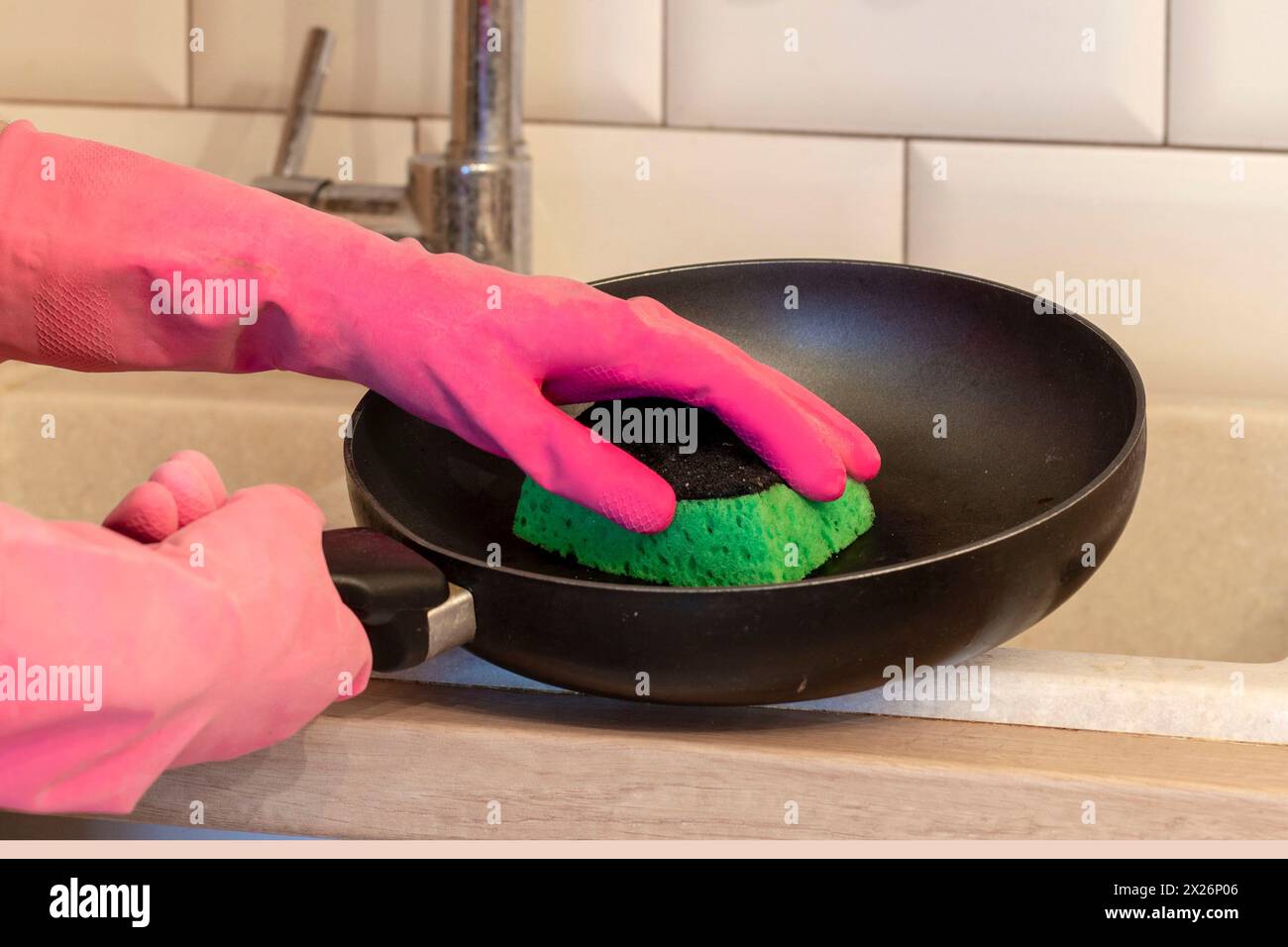 Cleaning a dirty frying pan with a kitchen sponge in the glove. Female ...