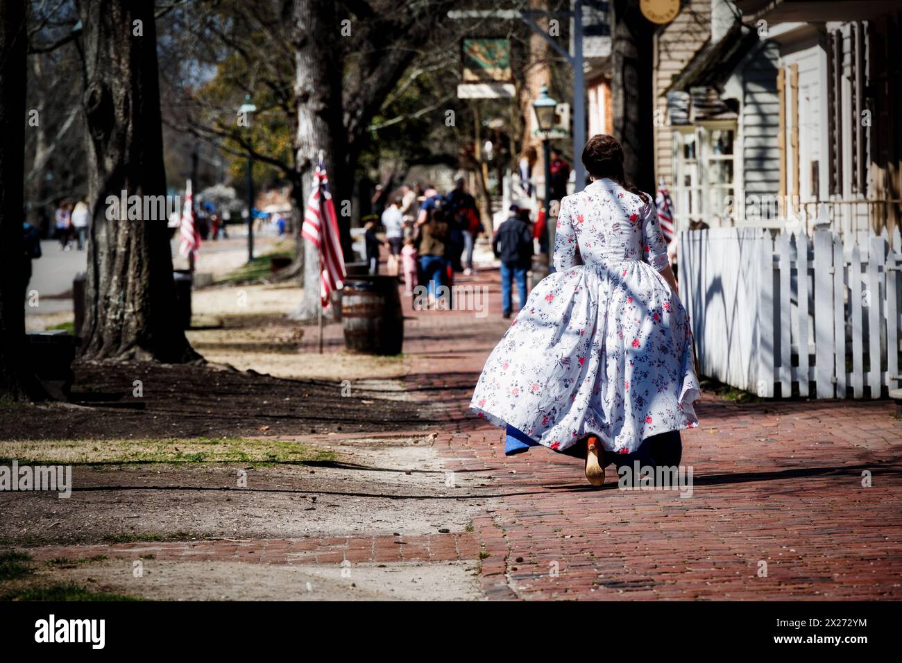 A woman, in period dress, walks behind tourists on East Duke of ...
