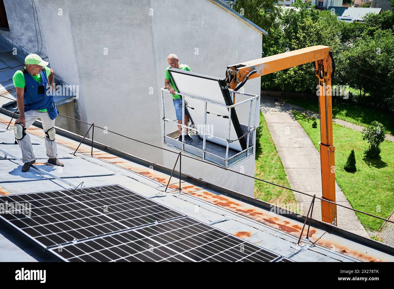 Workers lifting up photovoltaic solar panel on metal rooftop of house ...