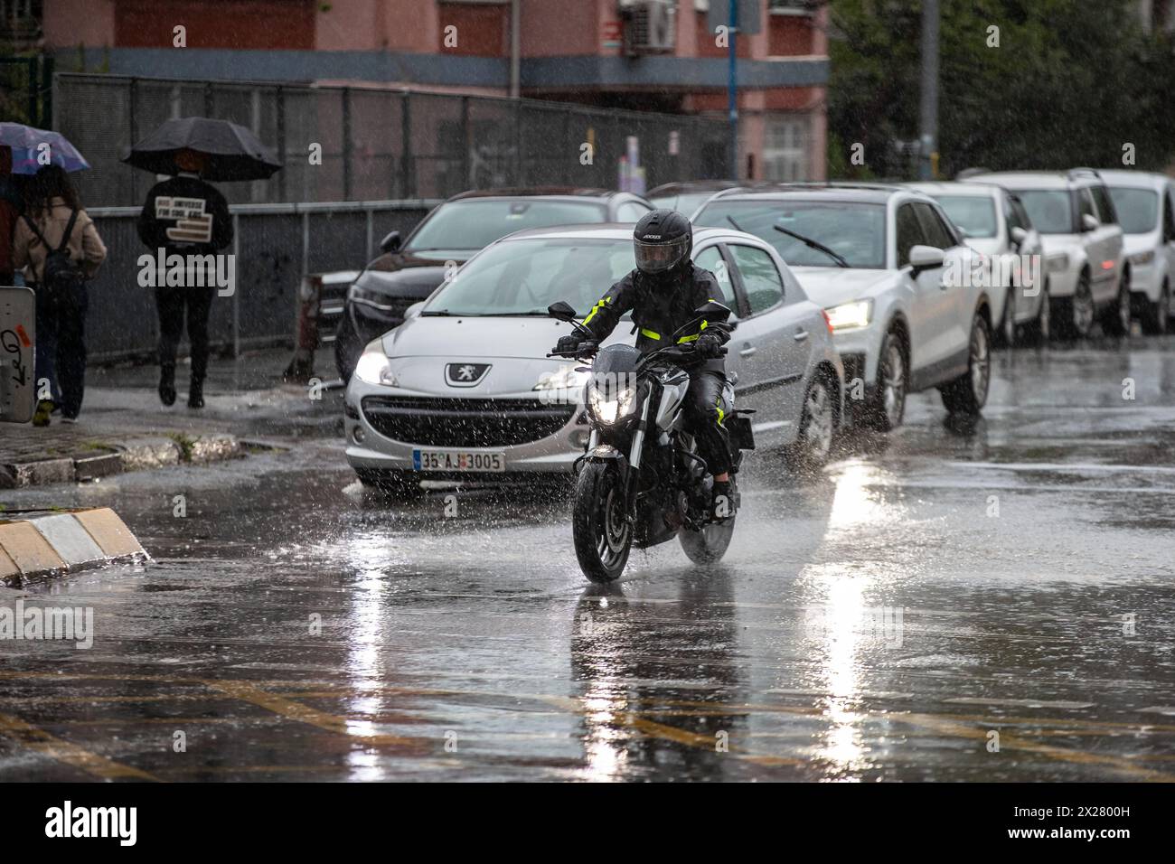 A man on a motor cycle at the traffic lights in Kadikoy under rain ...