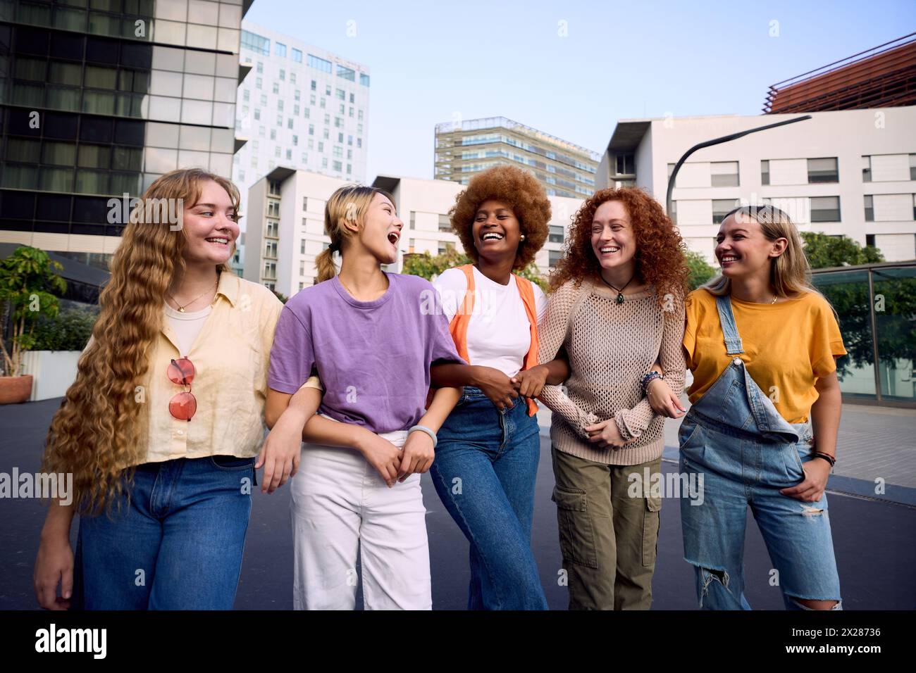 Multiracial group of smiling young gen z friends walking hugging on ...