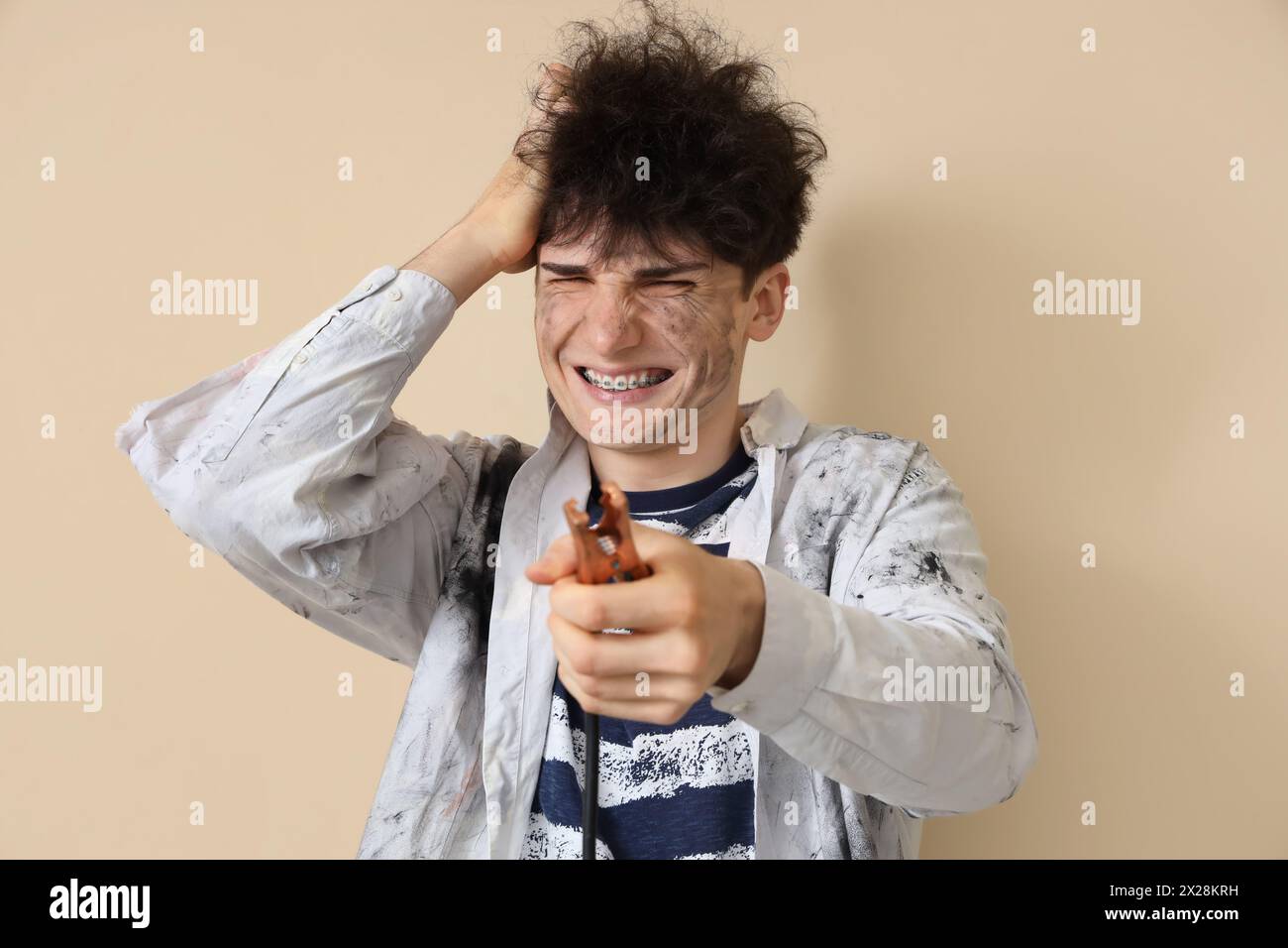 Electrocuted young man with burnt face and jumper cable on beige ...