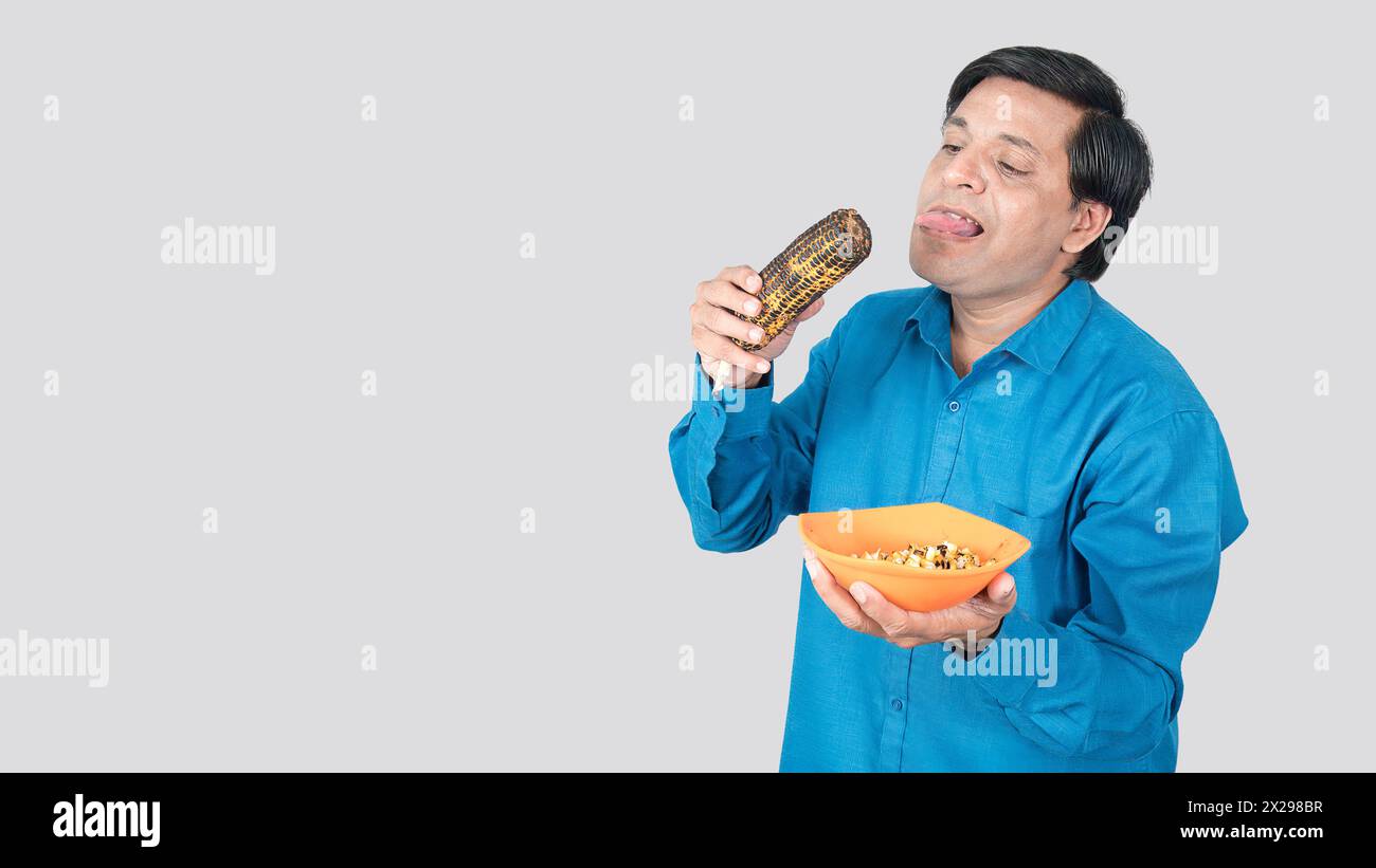 A young man looks desperate to eat a cob of corn in his hand and is ...