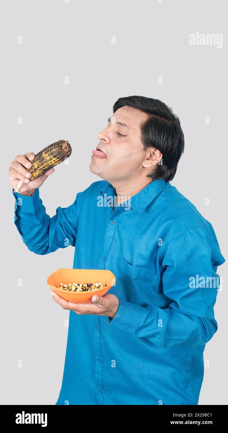 Portrait view of A young man looks desperate to eat a cob of corn in ...