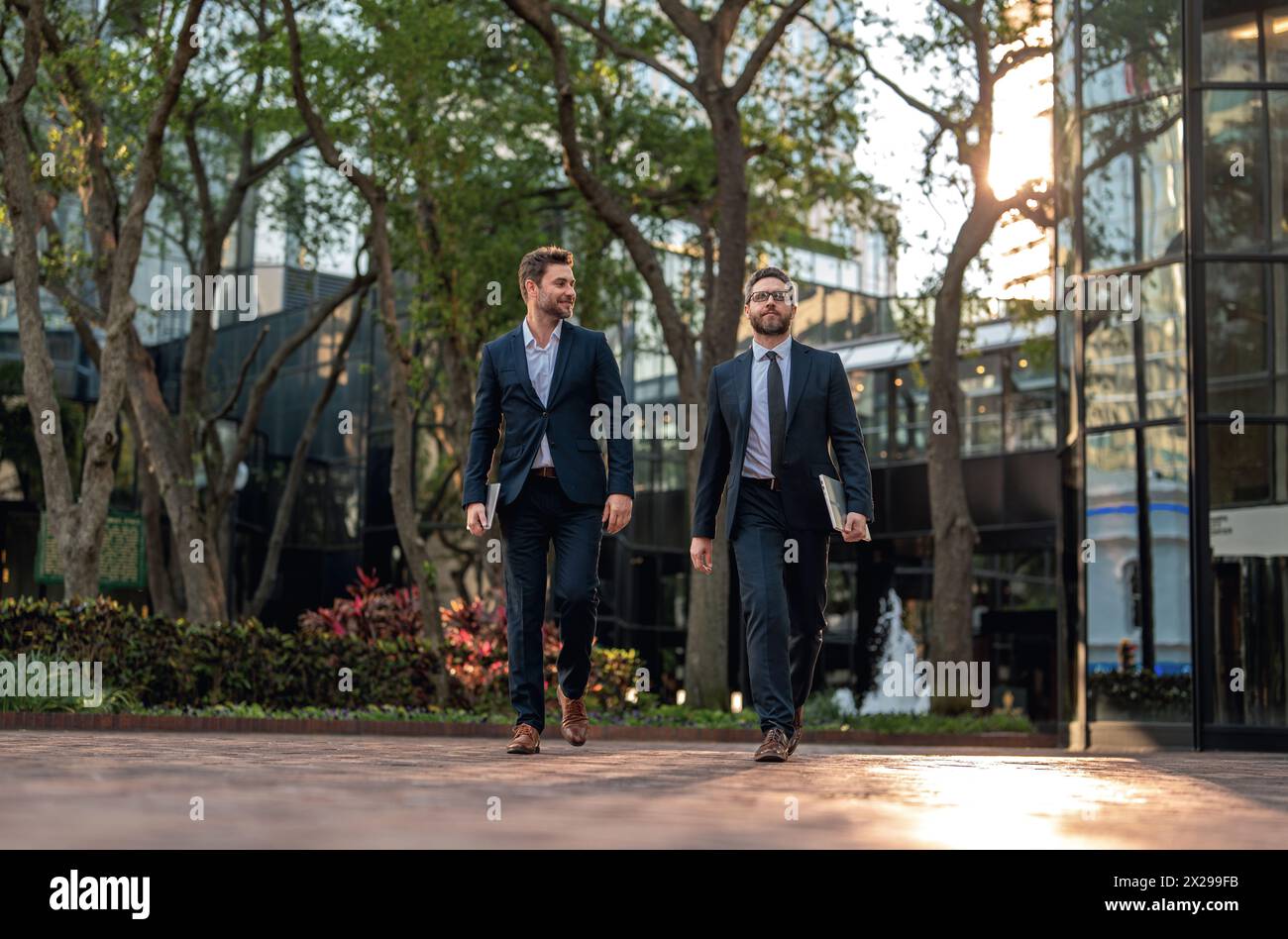 Photo of businessmen in suits walking outdoor through city street. Two ...