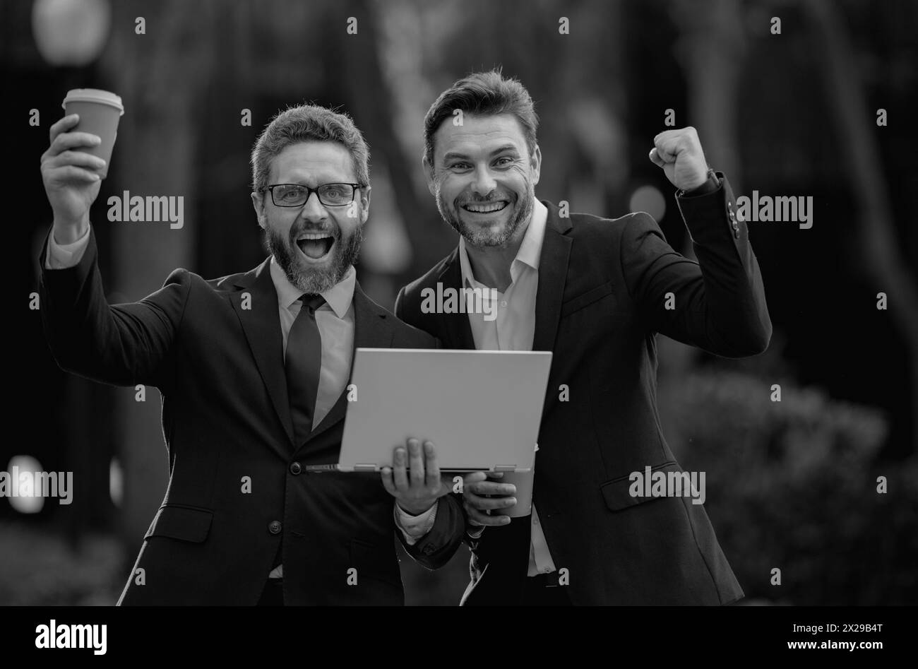 Two excited business men team using laptop outdoor. Amazed businessmen ...