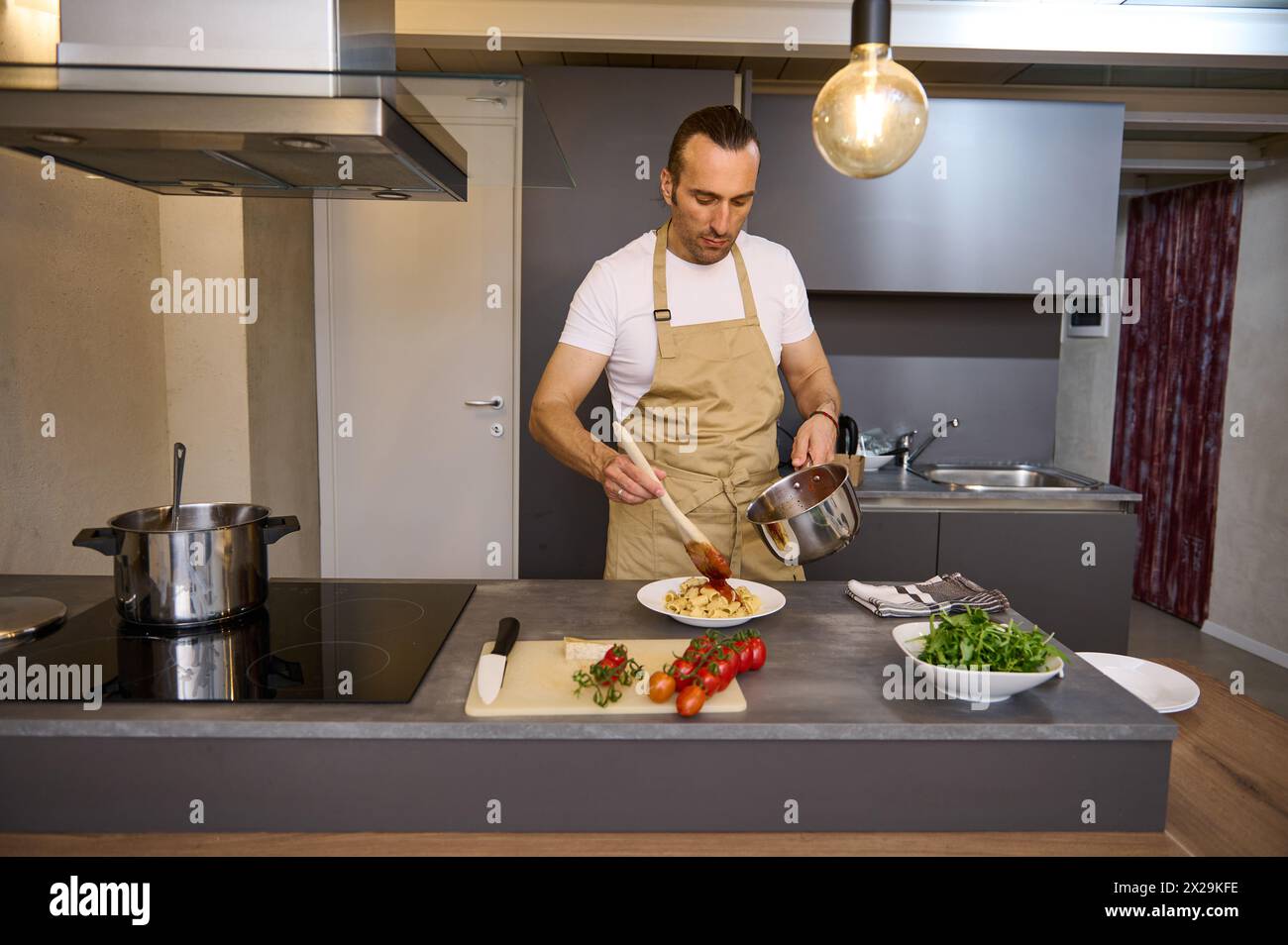 Attractive handsome European man in chef apron, pouring tomato sauce on ...