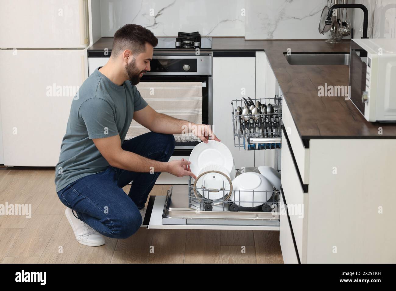 Smiling man loading dishwasher with plates in kitchen Stock Photo - Alamy