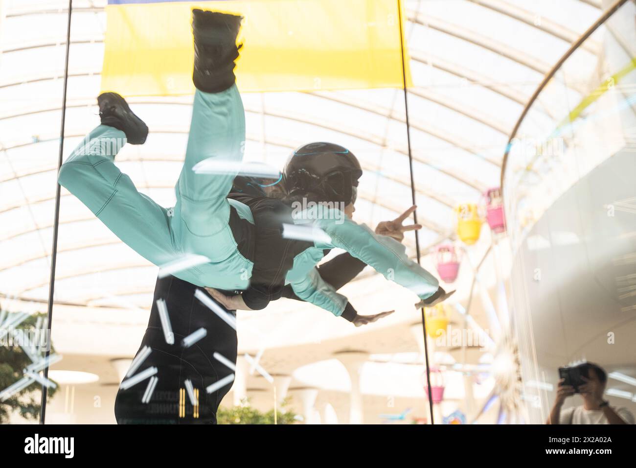 Excited teenage girl in helmet flying in aerodynamic tube wind tunnel ...