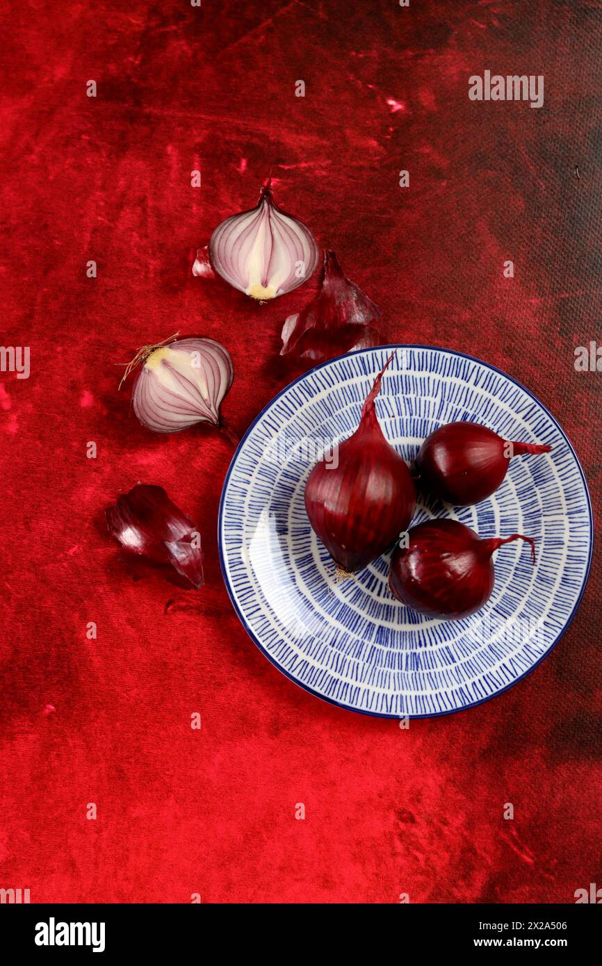 Red onion on blue ceramic plate, vibrant red textured background with ...