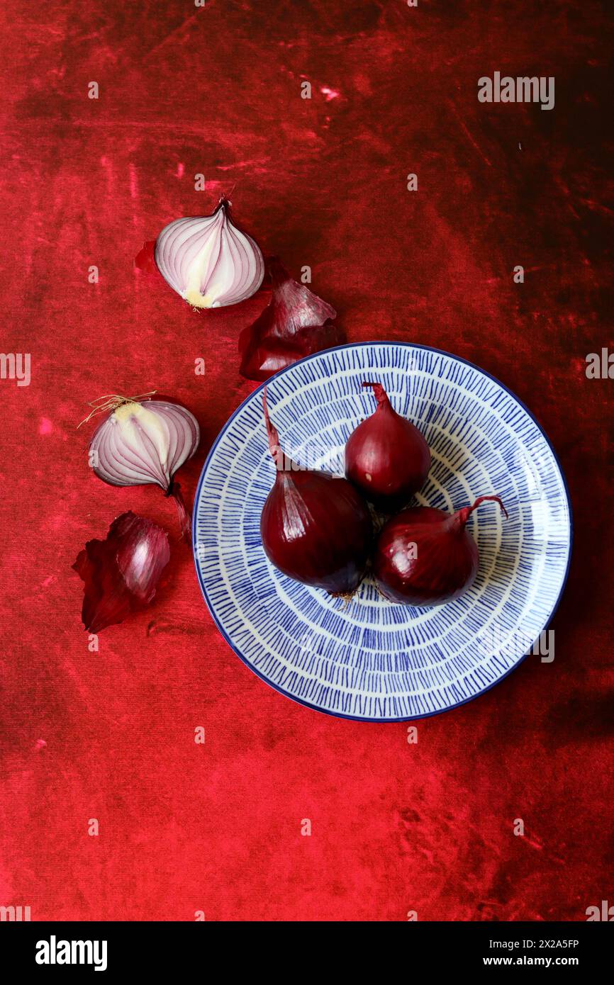 Red onion on blue ceramic plate, vibrant red textured background with ...