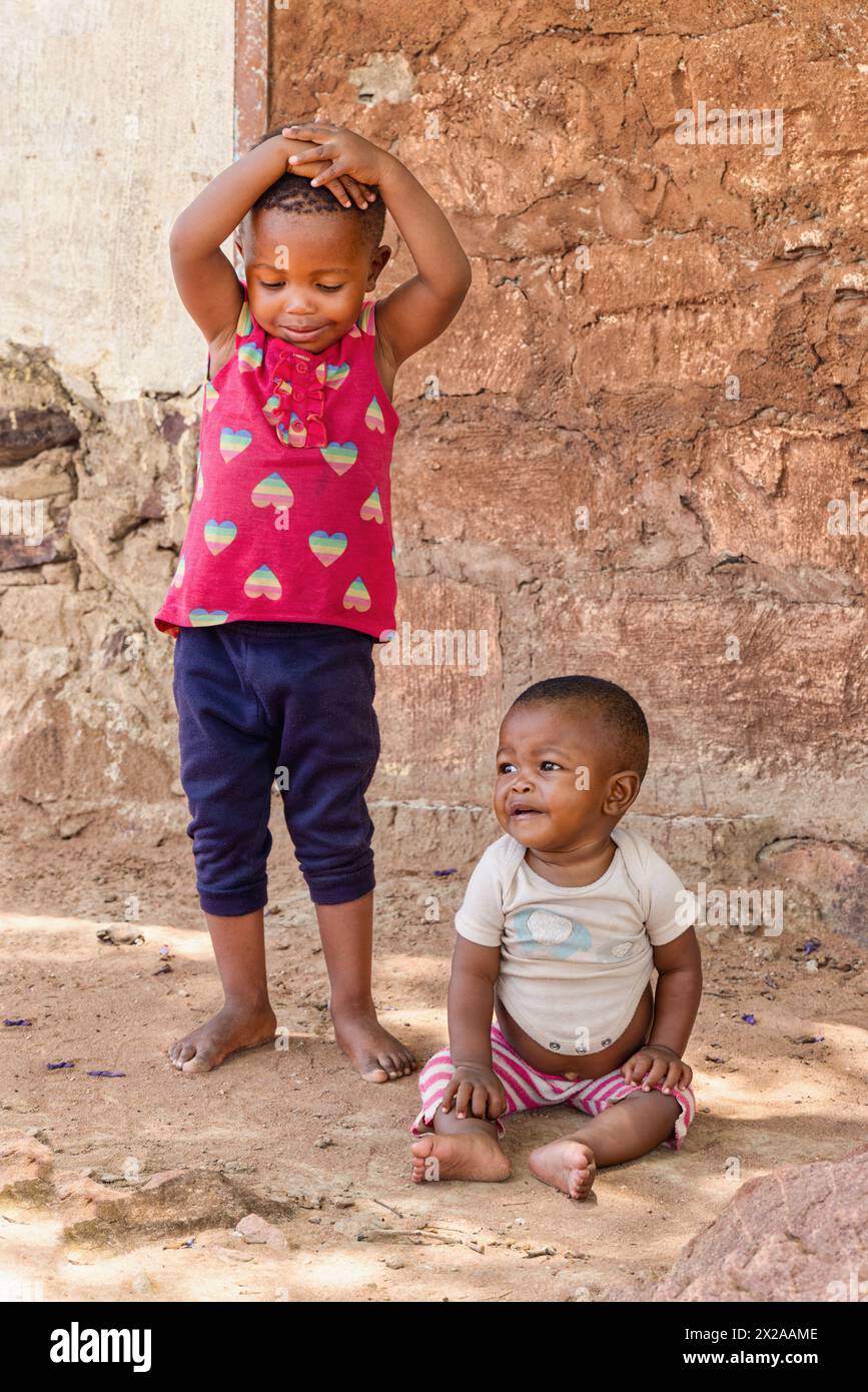 two african villager children playing outdoors in front of the house in ...