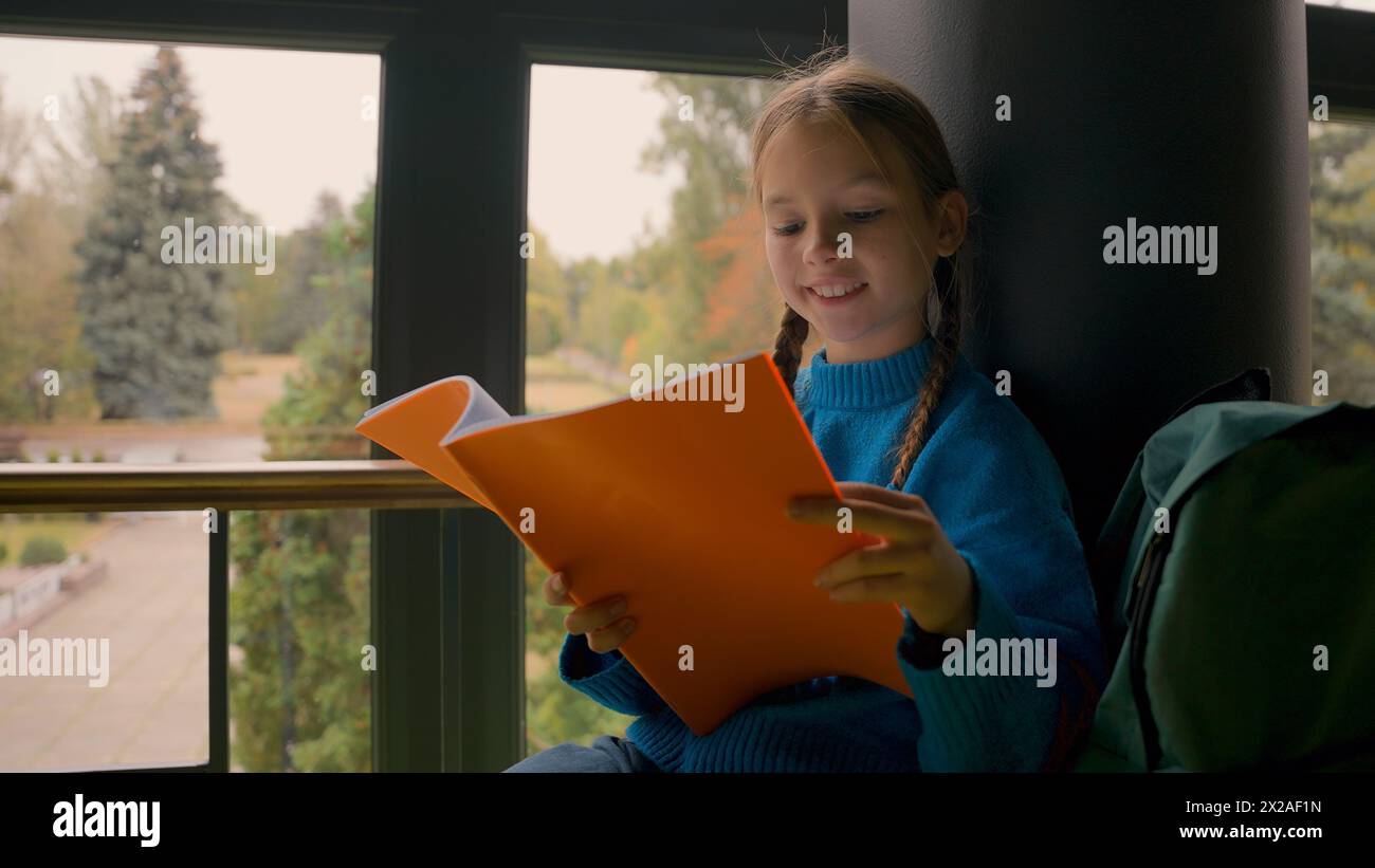 Little girl sitting school hall reading textbook prepare exam task ...