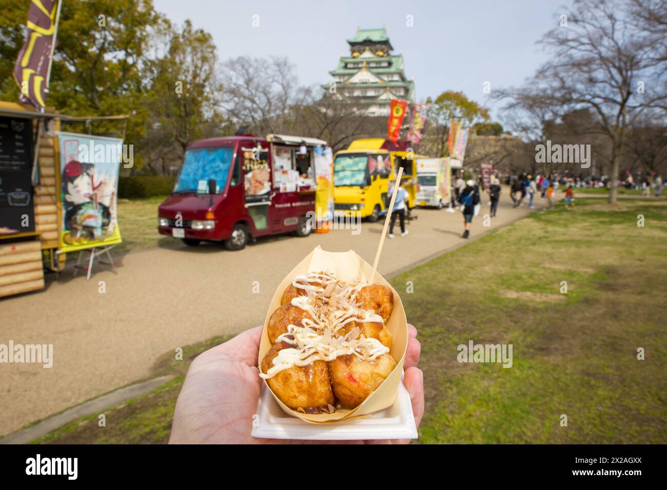 one hand holds a bowl of takoyaki, a famous Osaka dumpling, with food ...