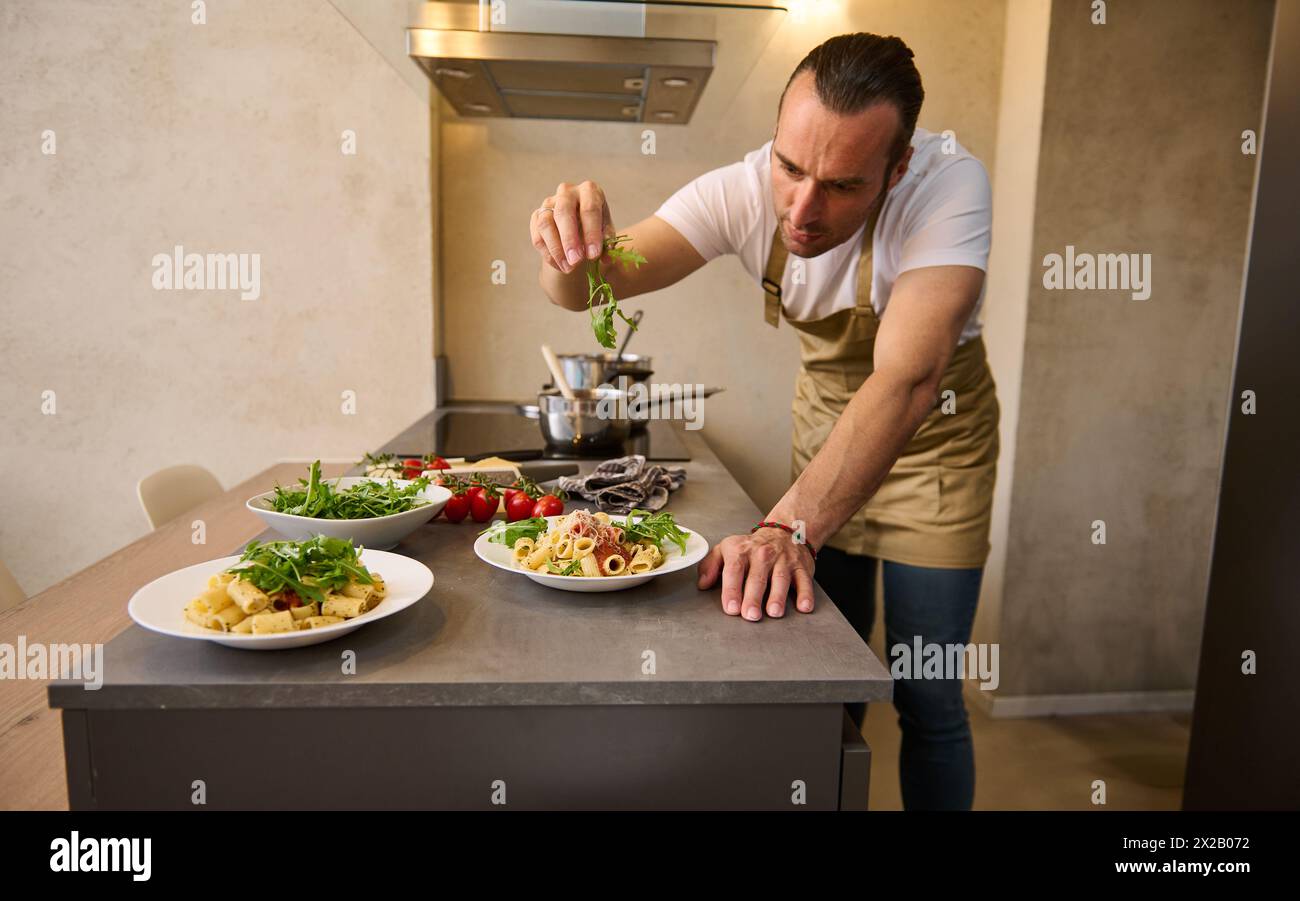Attractive European male chef decorating spaghetti Bolognese with fresh ...