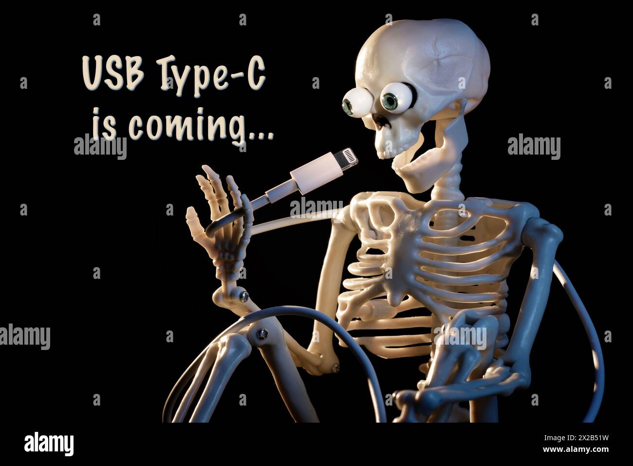 Funny Skeleton toy holding a USB lightning cable, in black background ...