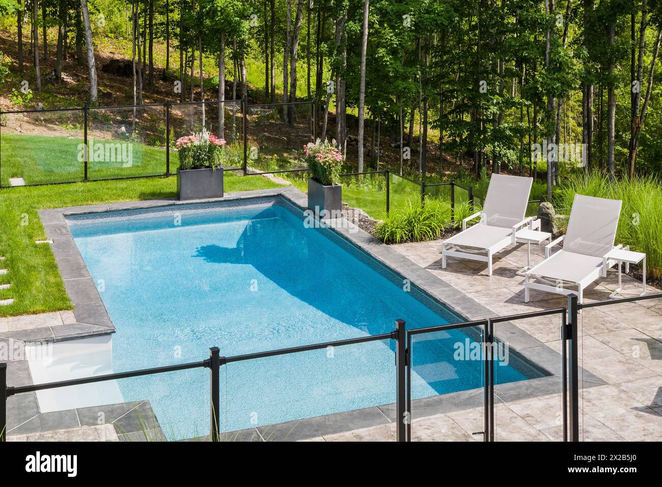 Two white long chairs on edge of in-ground swimming pool enclosed by ...