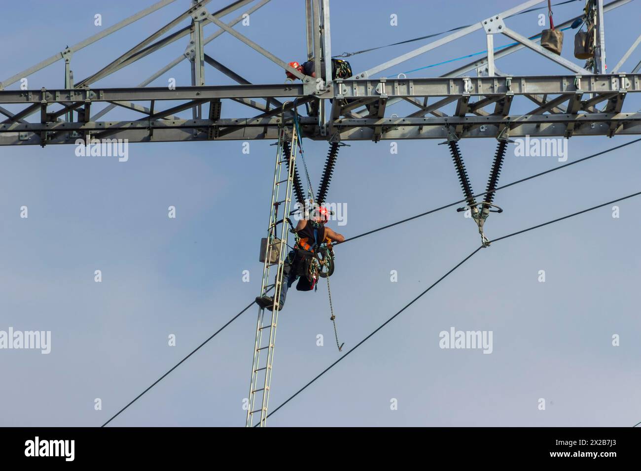 A technician works on a high-voltage pylon under a clear blue sky Stock ...