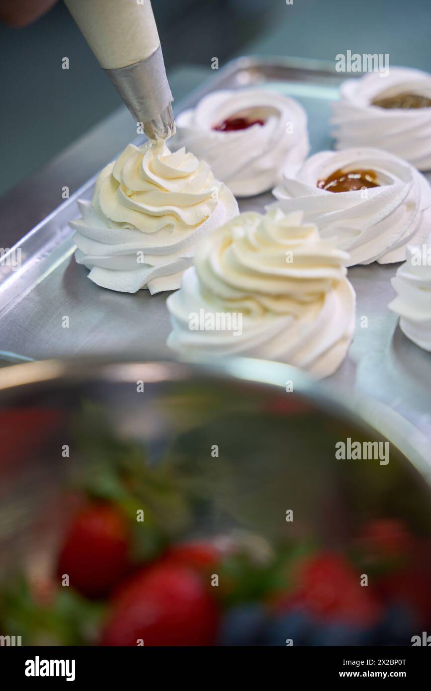 Baker adding custard from pastry bag at top of merengue nest Stock ...