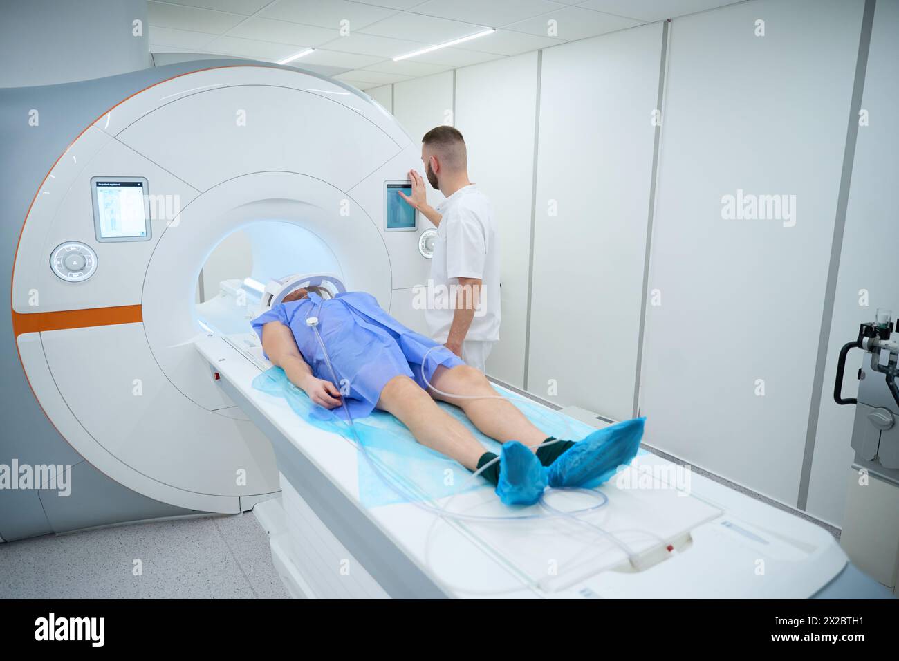 Medical professional positioning man for contrast-enhanced brain MRI ...