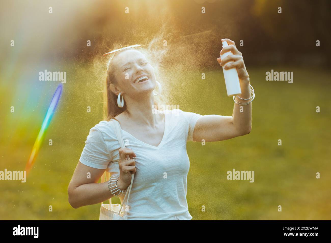 Summer time. happy modern female in white shirt using face spray in the ...
