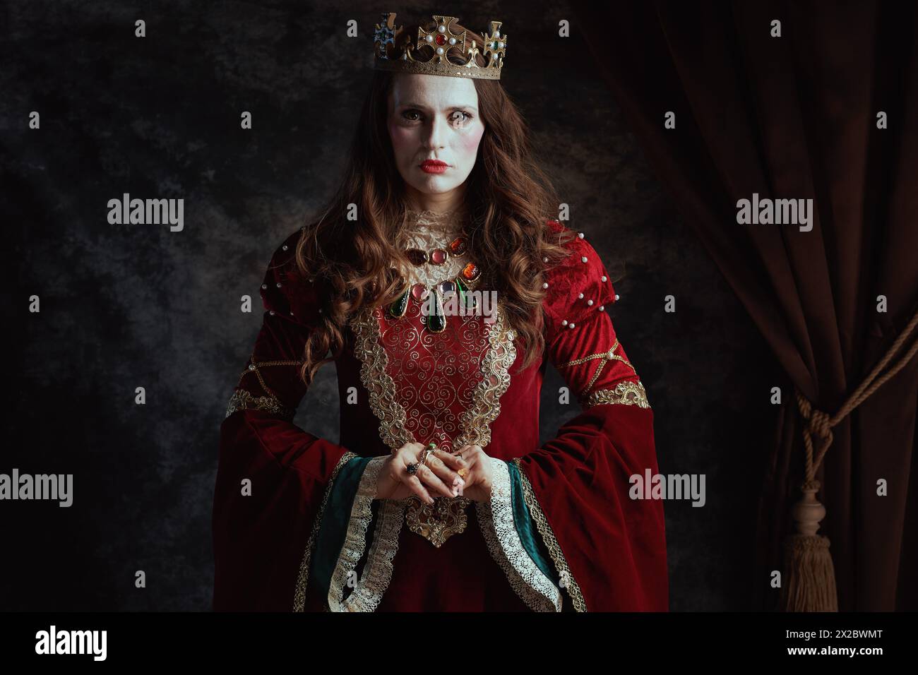 medieval queen in red dress with white makeup and crown on dark gray ...