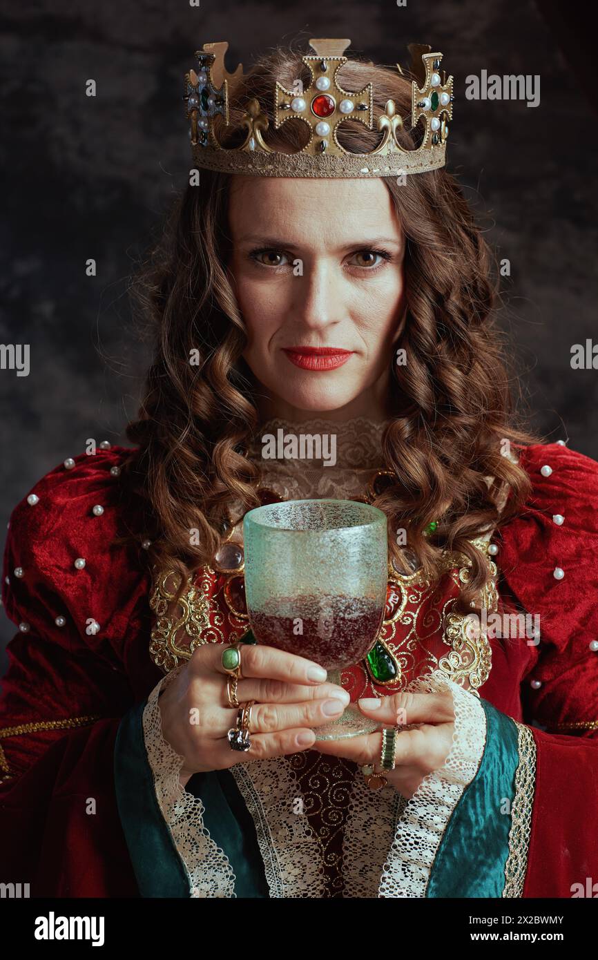 medieval queen in red dress with goblet and crown on dark gray ...