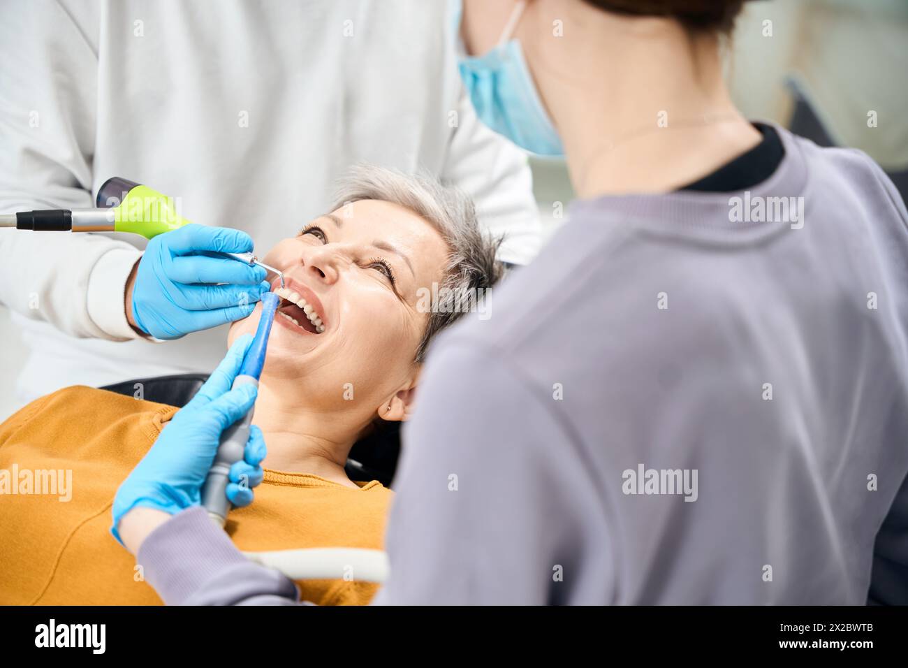 Woman smiling while dentist keeping out procedure of airflow teeth ...
