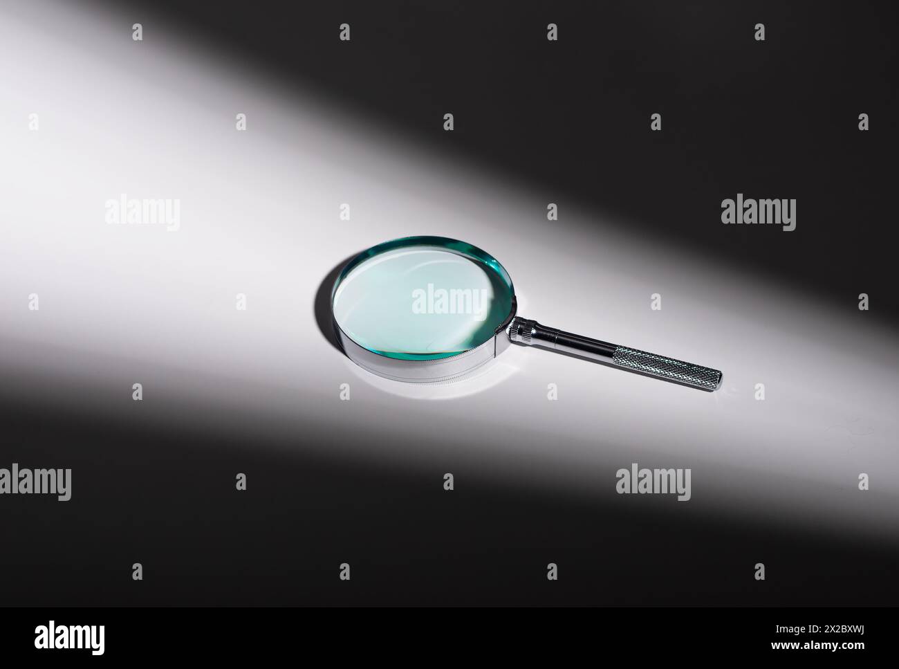 Silver magnifying glass on glass surface, shadow and light play ...