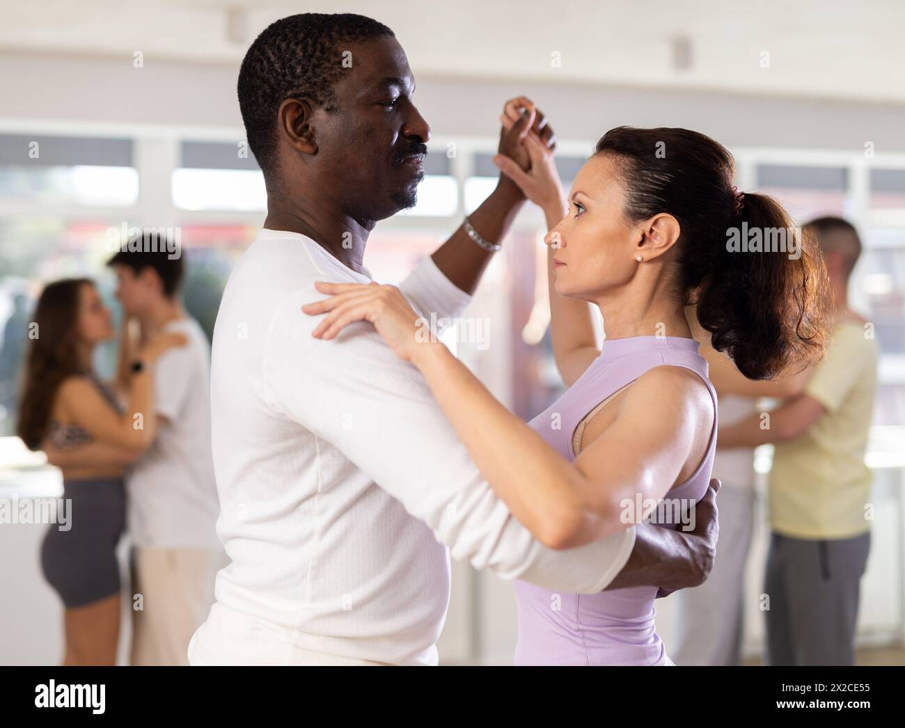 Pretty young woman dancing waltz with african american partner at group ...