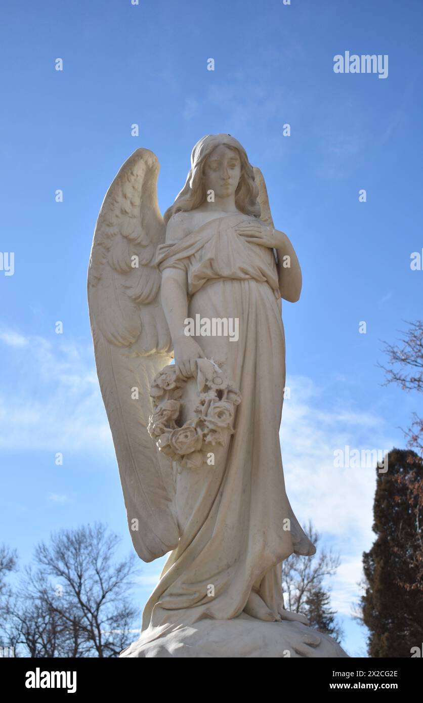 carved angel statue standing in a beautiful cemetery with a blue sky ...