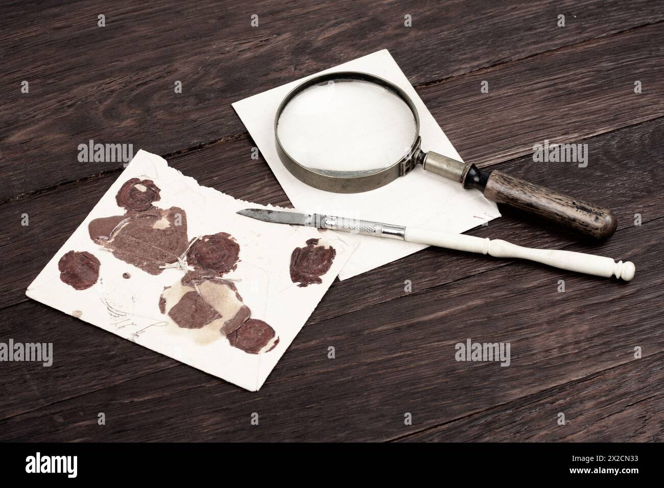 Retro envelope opener knife with magnifying glass and vintage letter envelope on wooden desk ...