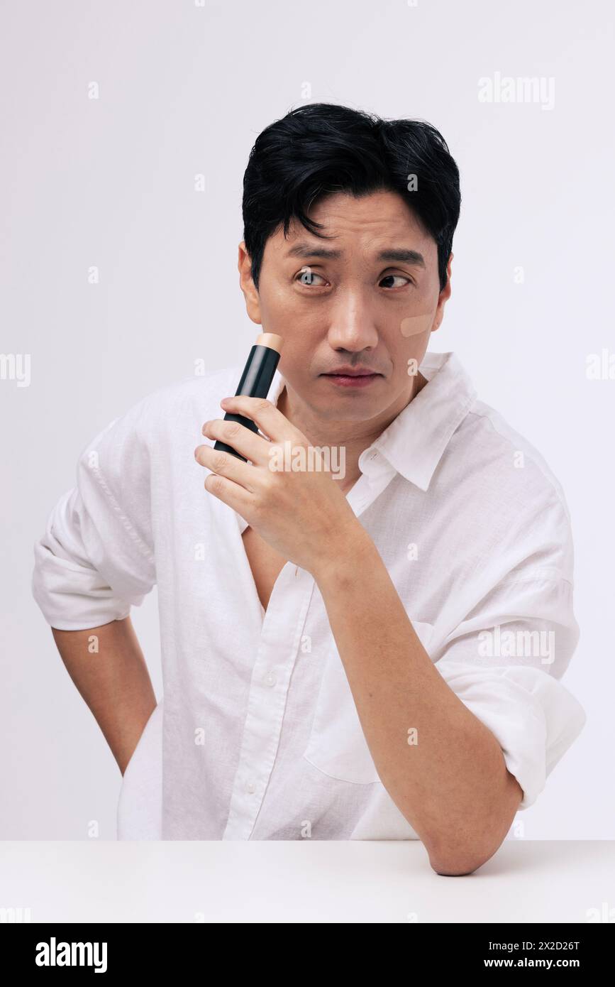 a middle aged man wearing a white shirt and putting foundation on his ...