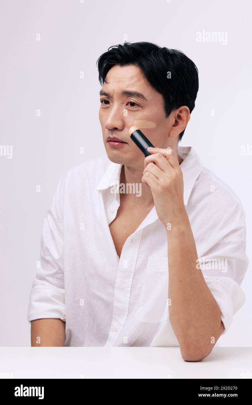 a middle aged man who puts foundation on his face against a white ...