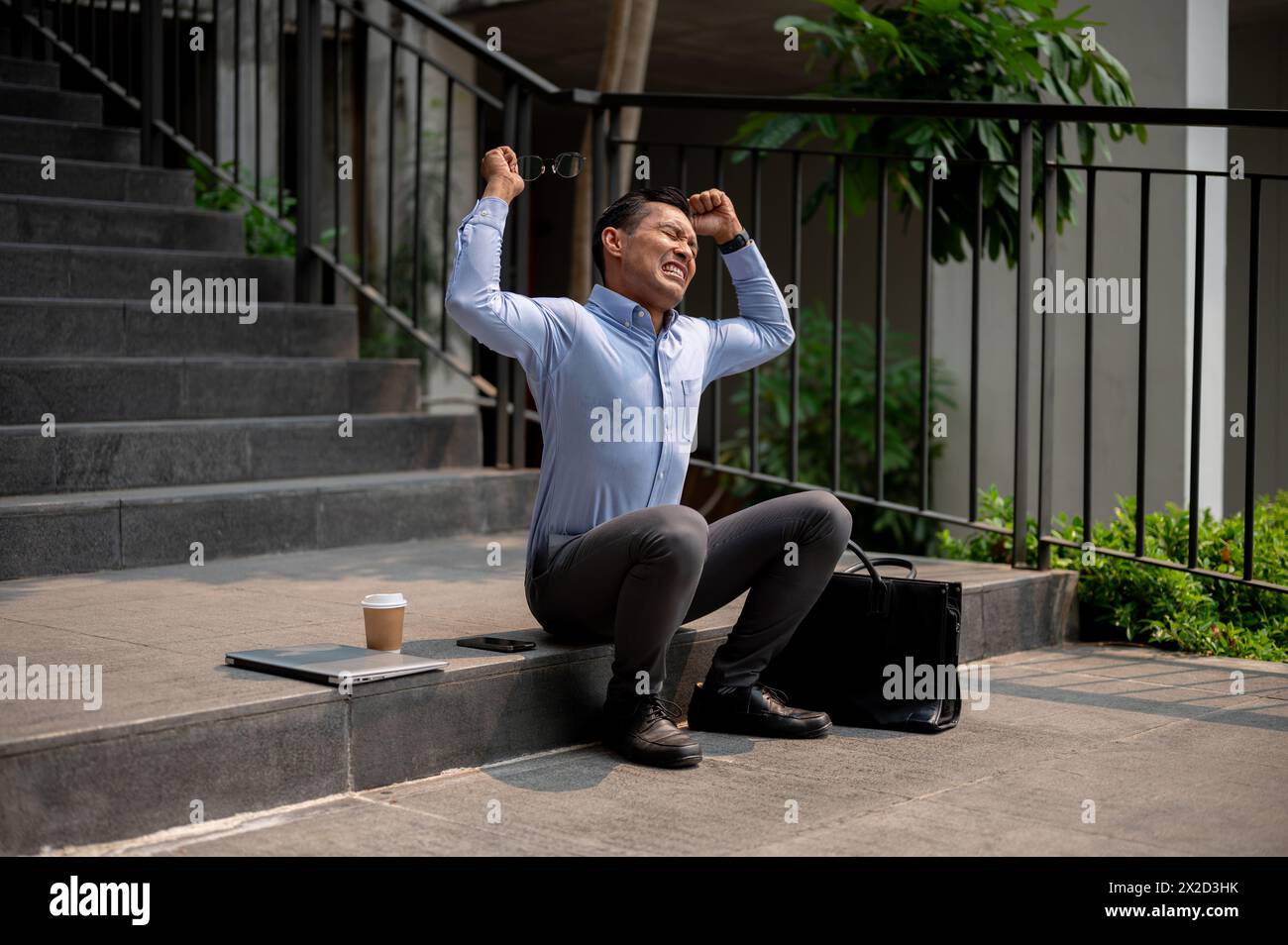 An angry, stressed Asian businessman sits on outdoor steps, crying ...