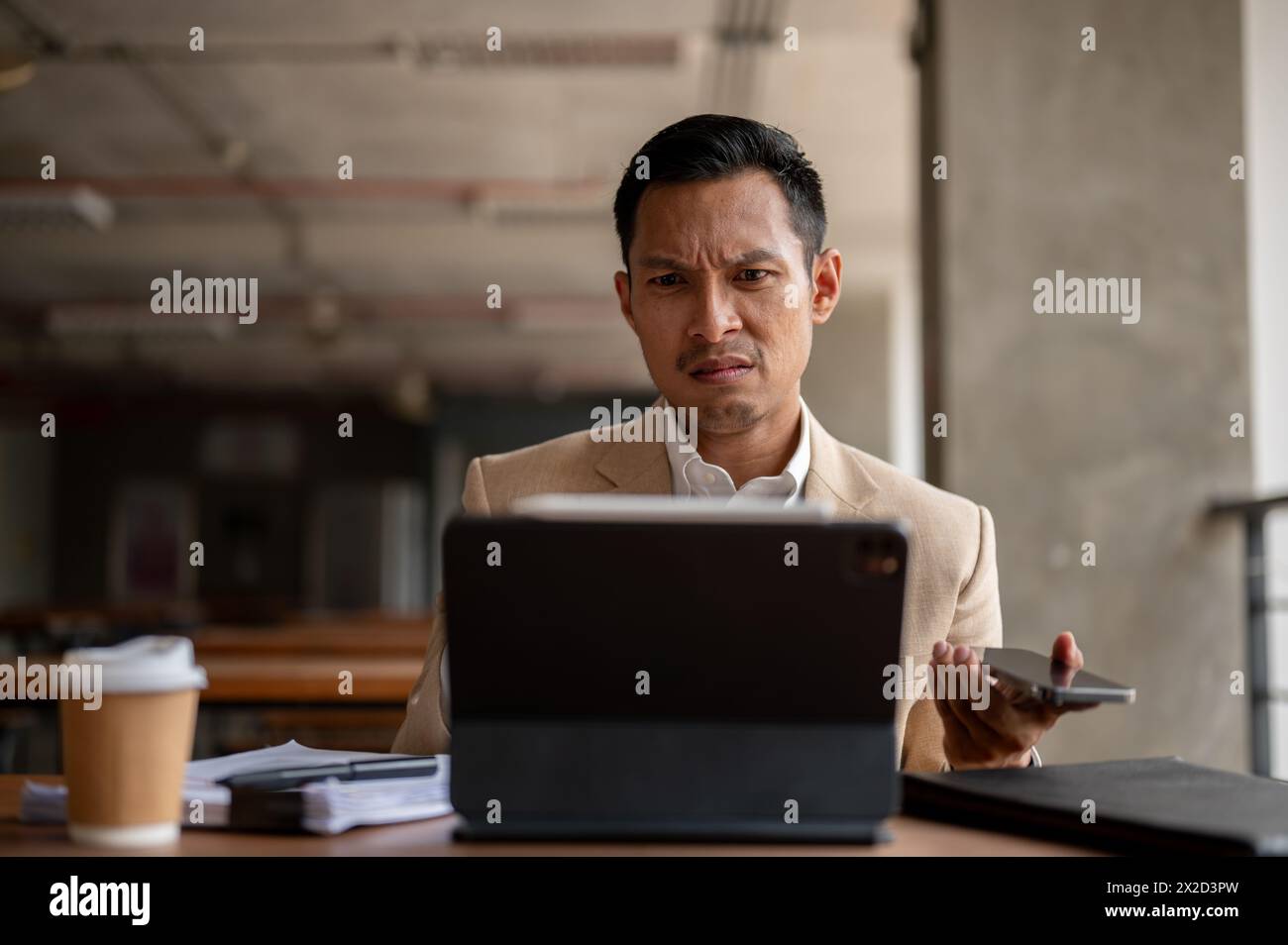 A confused, serious-looking Asian millennial businessman is staring at ...
