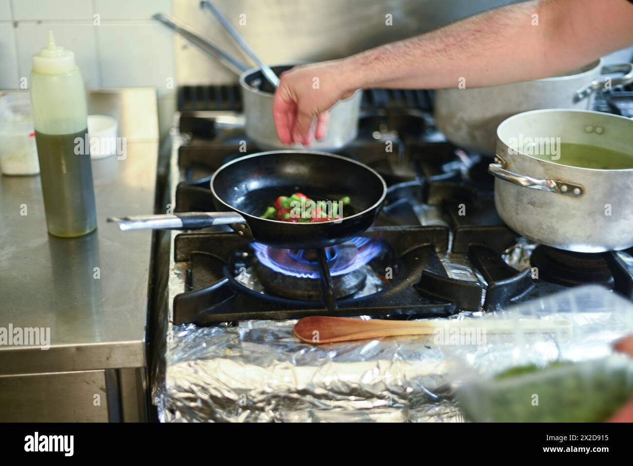 A man is cooking food in a pan on a stove. The pan is on a burner that ...