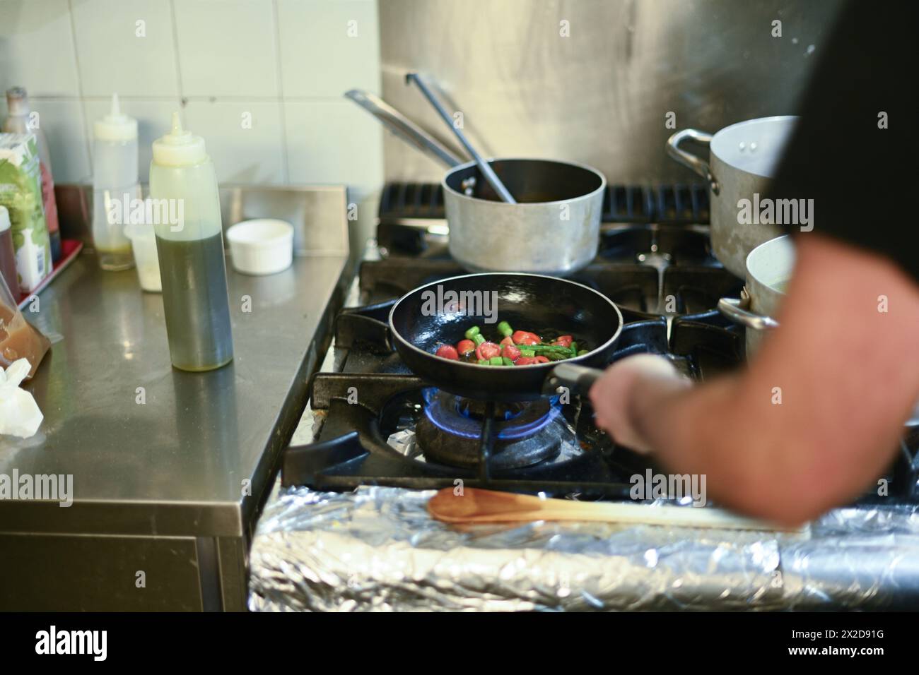 A man is cooking food in a pan on a stove. The pan is on a burner that ...