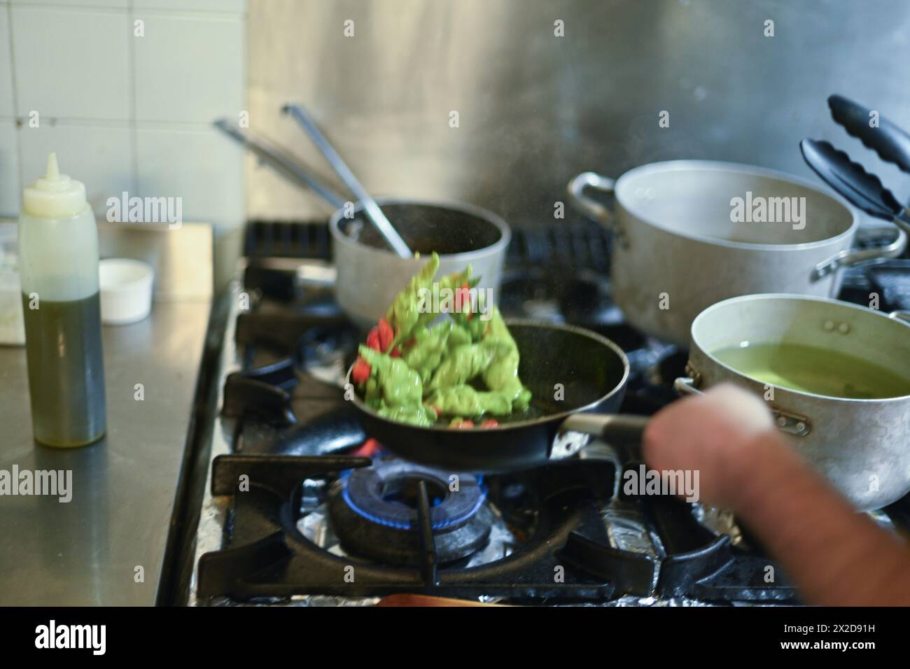 A man is cooking food on a stove with a bottle of oil next to him ...