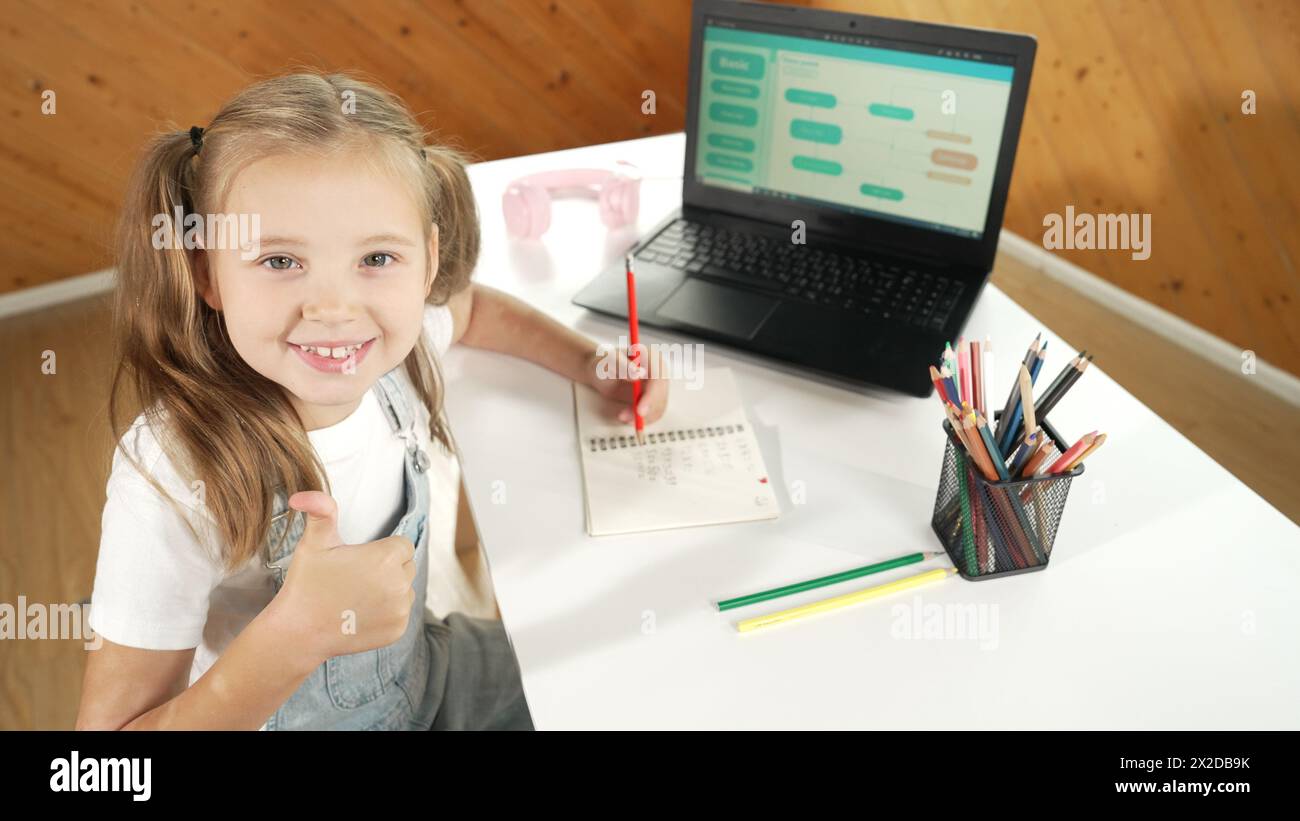 Little pretty caucasian girl doing classwork while showing a thumb up ...