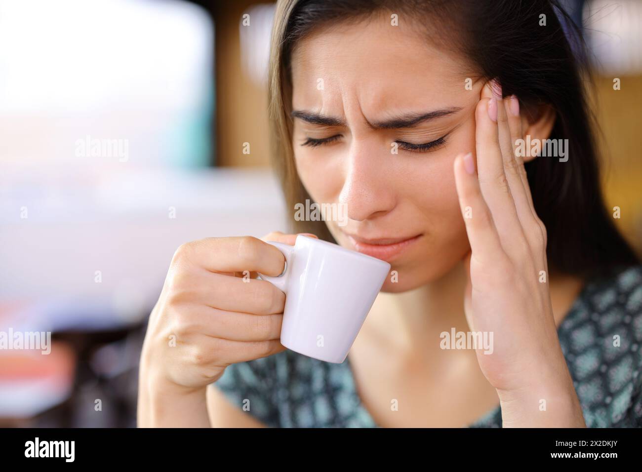 Worried woman drinking coffee suffering head ache in a bar interior ...