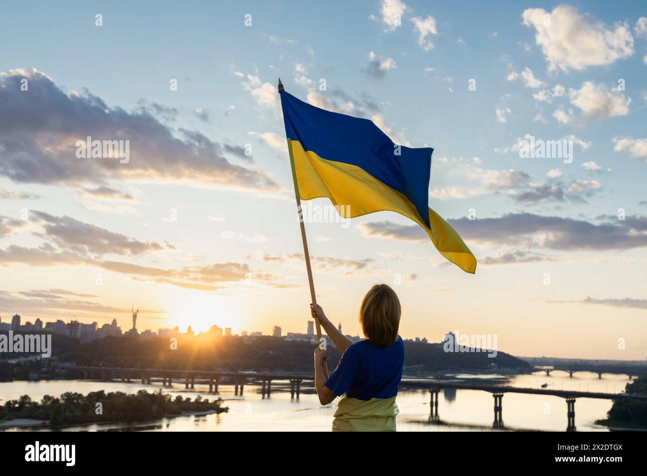 sunset over the city of Kyiv. a woman holds a large waving Ukrainian ...